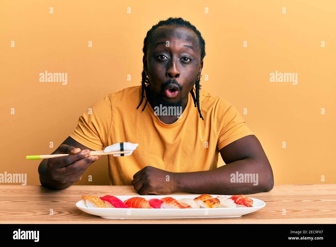 Handsome young black man eating sushi sitting on the table scared and ...