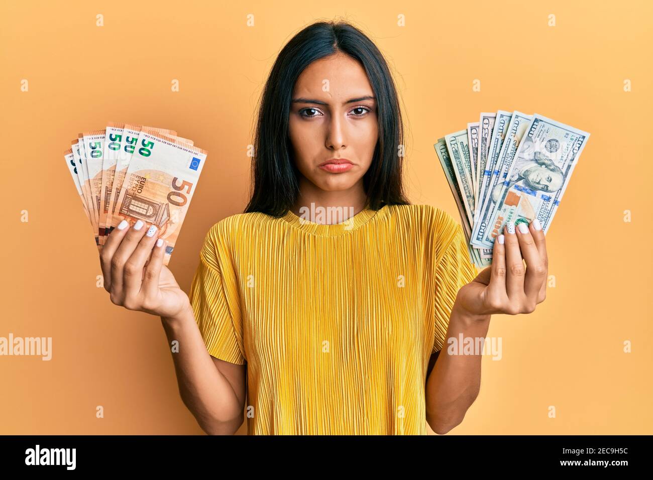 Young brunette woman holding bunch of dollars and euros depressed and ...