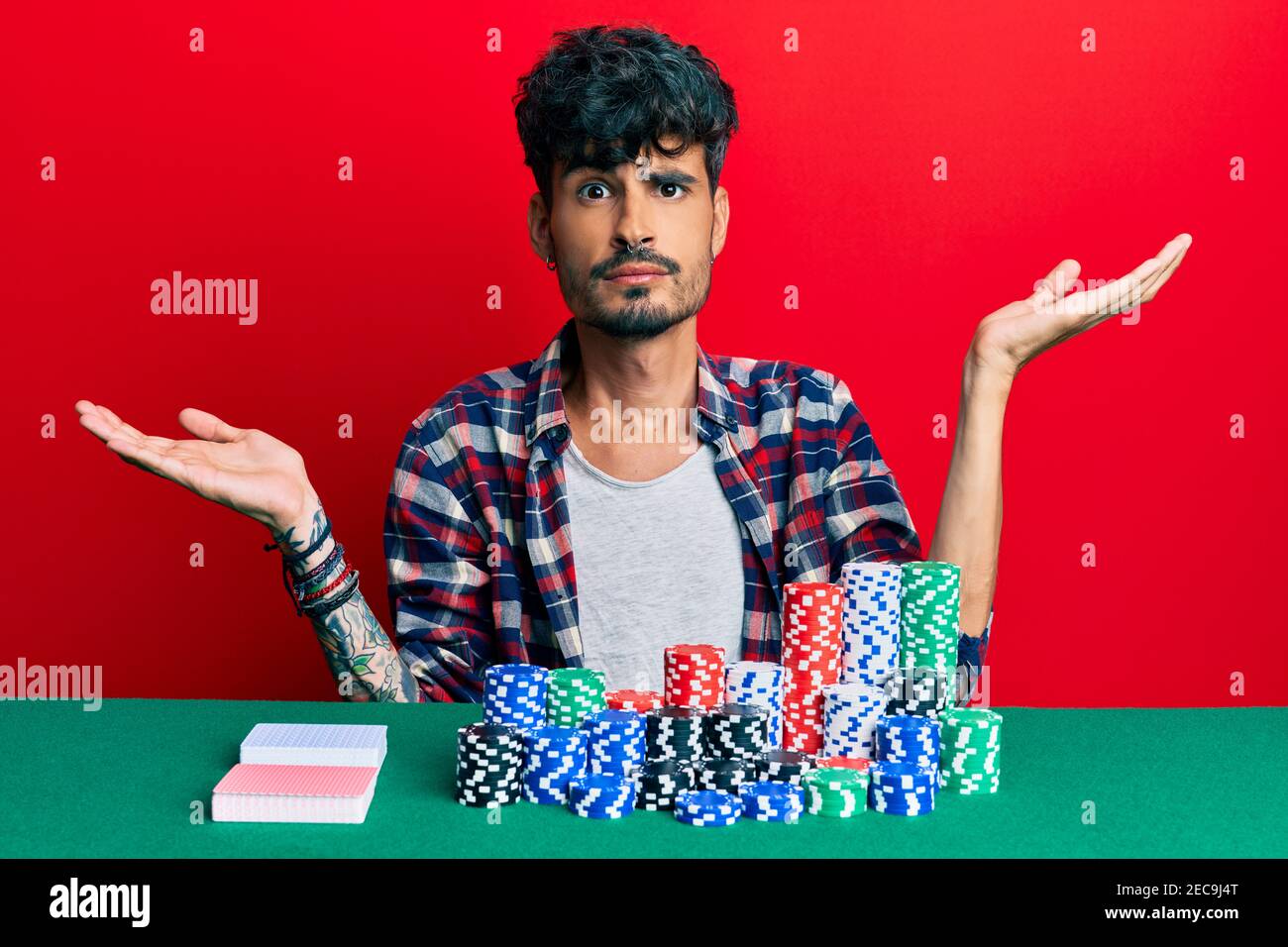 Young hispanic man sitting on the table with poker chips and cards ...