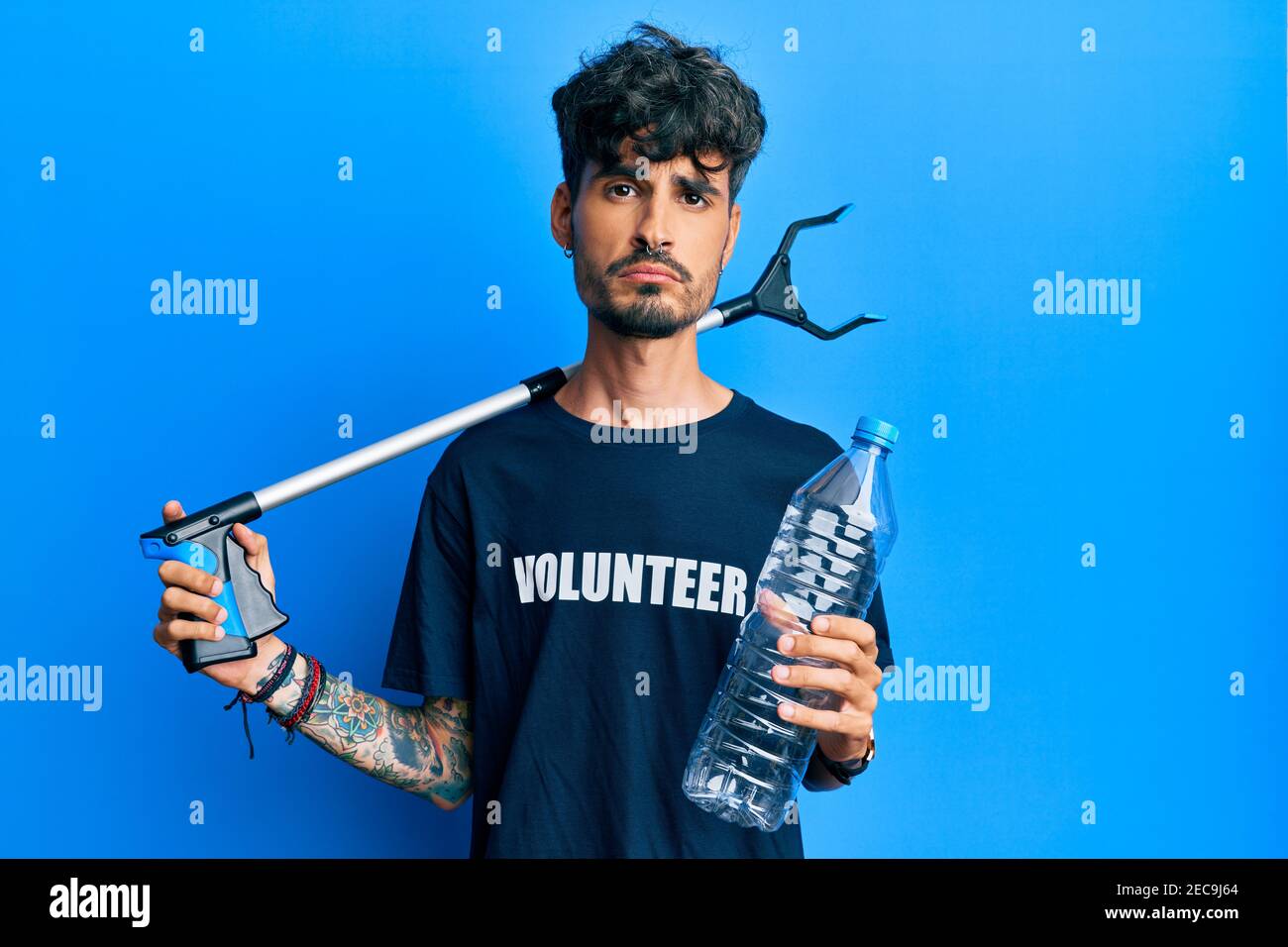Young hispanic man holding plastic bottle and litter picker to recycle ...