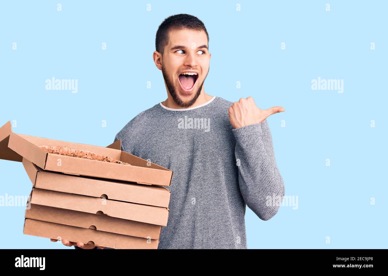 Young handsome man holding delivery italian pizza boxes pointing thumb ...