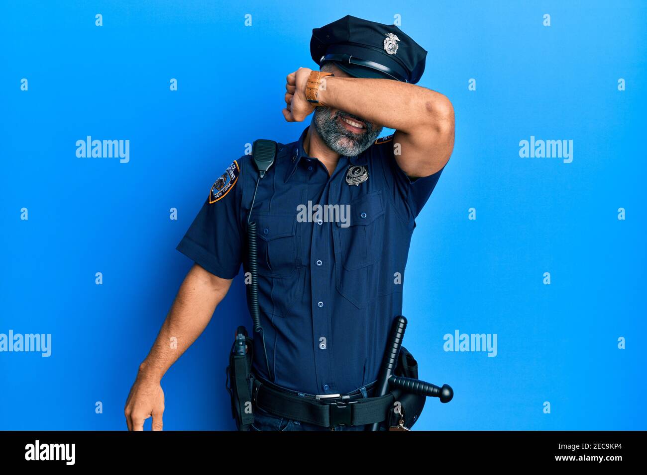 Middle age handsome man wearing police uniform covering eyes with arm ...