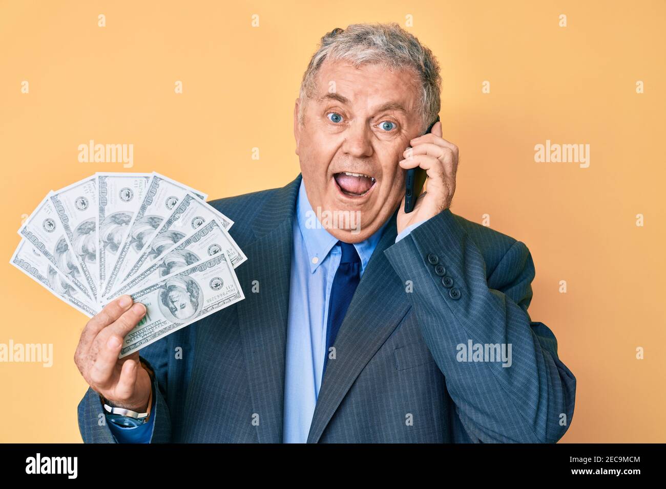 Senior grey-haired man wearing suit holding dollars and using ...