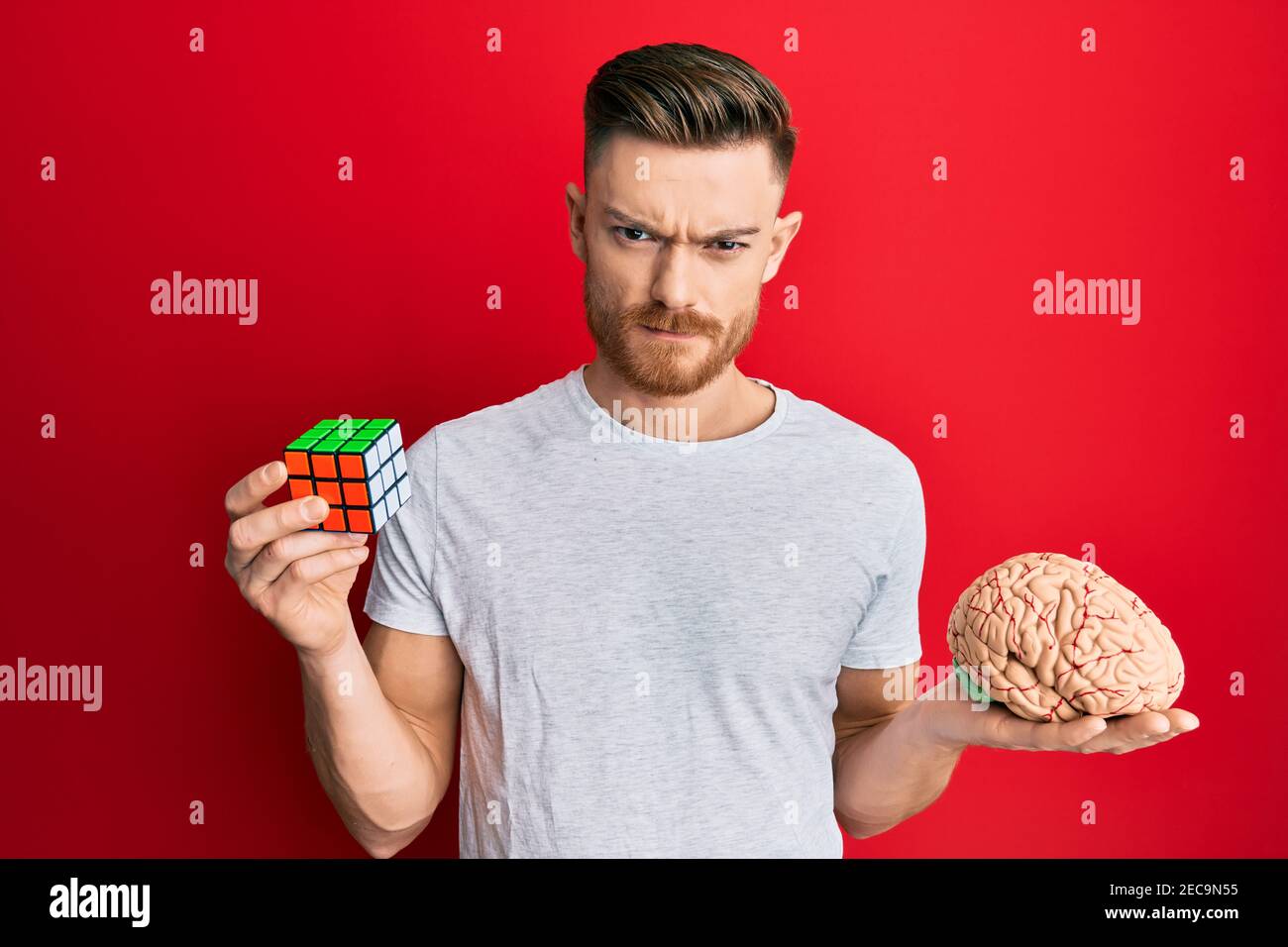 Young redhead man playing colorful puzzle cube intelligence game ...