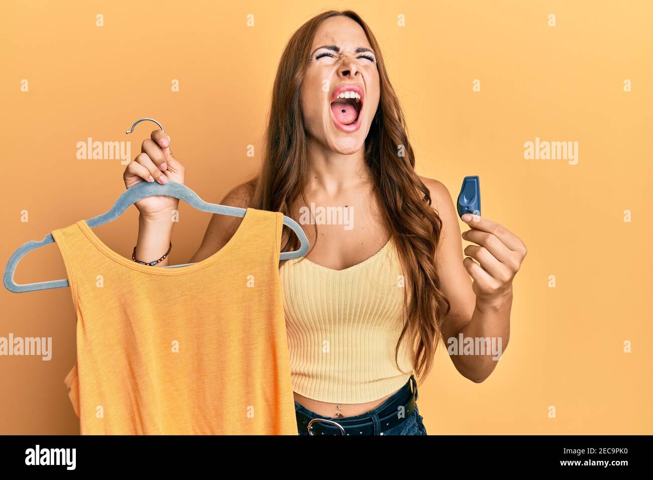 Young brunette shopkeeper woman holding clothes and security alarm ...