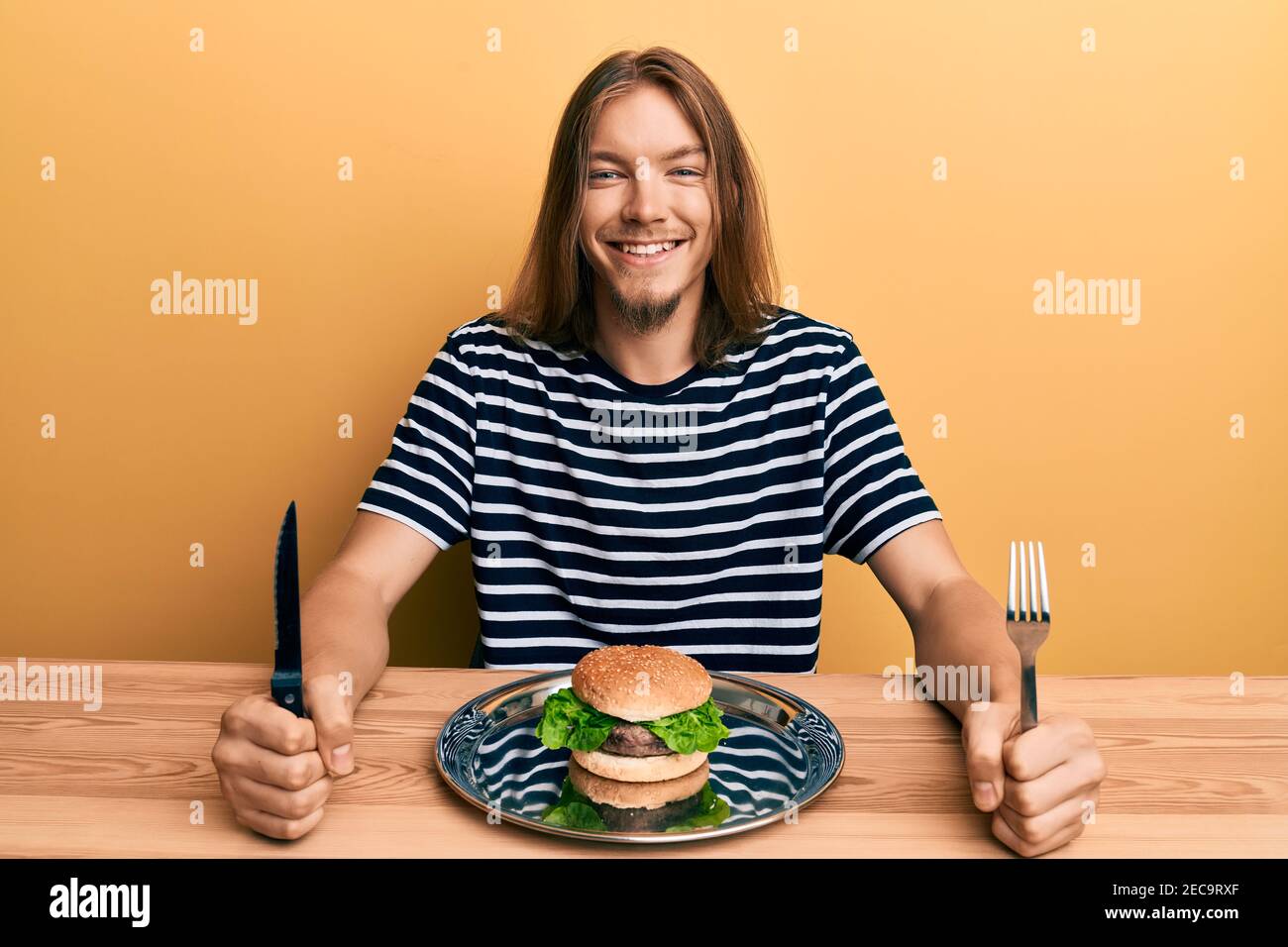 Handsome caucasian man with long hair eating a tasty classic burger ...