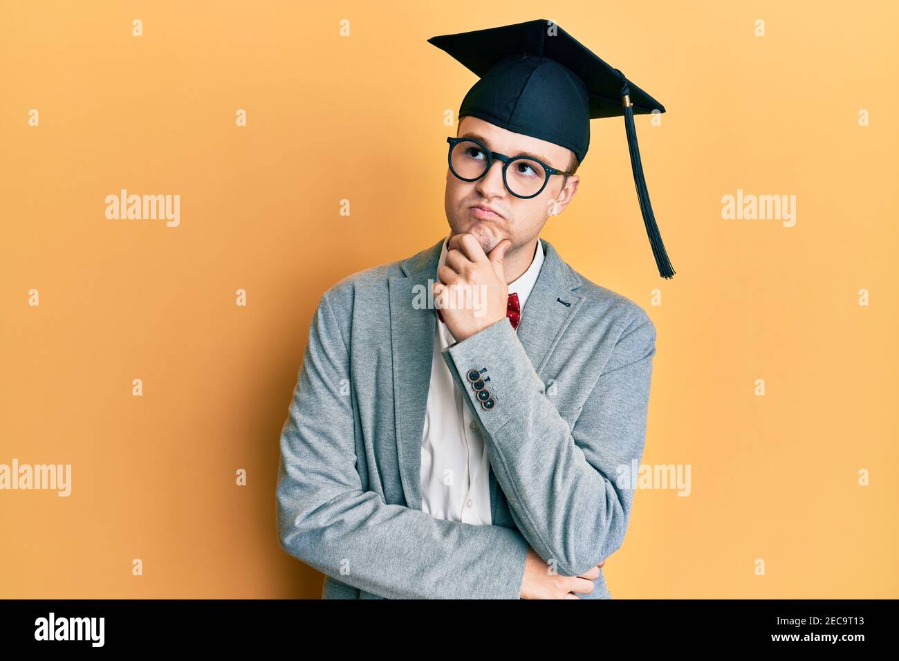 Young caucasian nerd man wearing glasses and graduation cap thinking ...