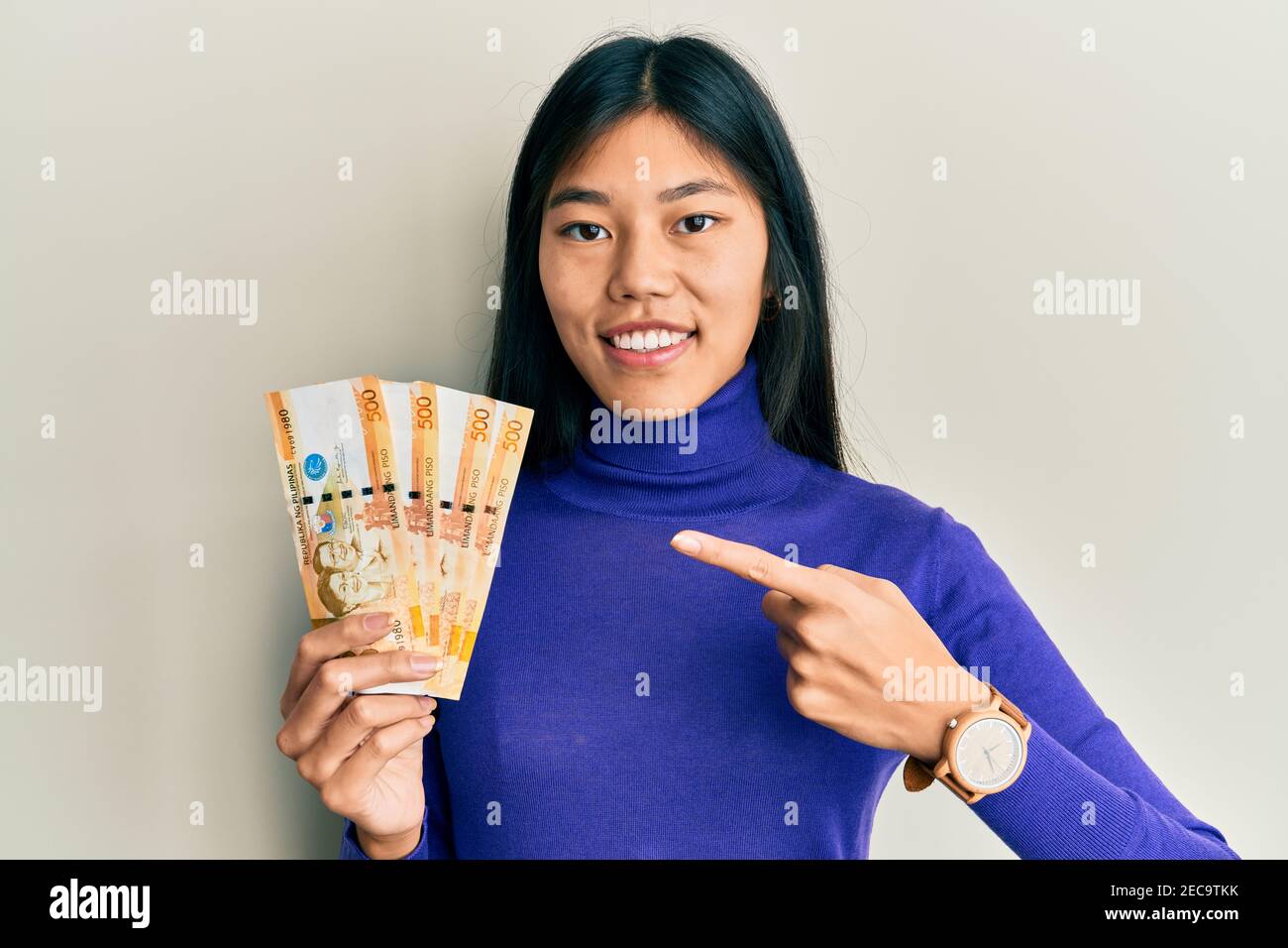 Young chinese woman holding 500 philippine peso banknotes smiling happy ...