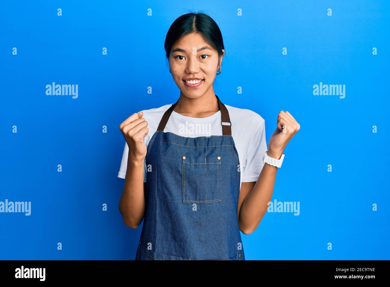 Young chinese woman wearing waiter apron celebrating surprised and ...