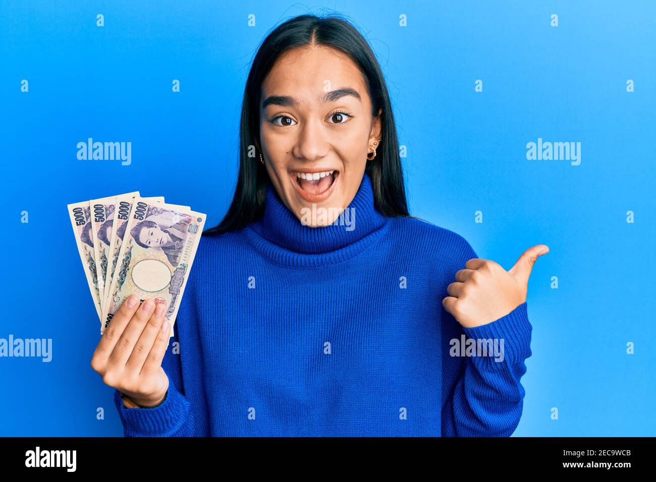 Young asian woman holding 5000 japanese yen banknotes pointing thumb up ...