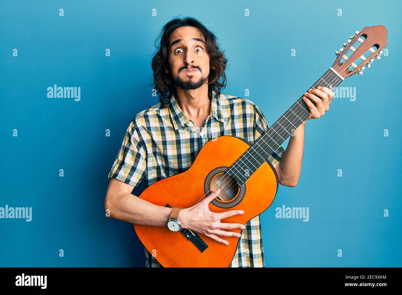 Young hispanic man playing classical guitar puffing cheeks with funny ...