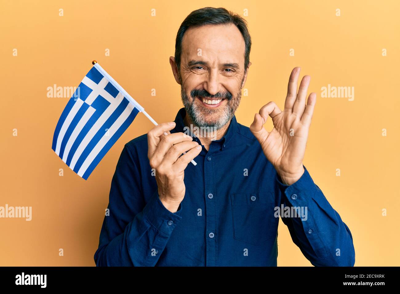 Middle age hispanic man holding greece flag doing ok sign with fingers ...