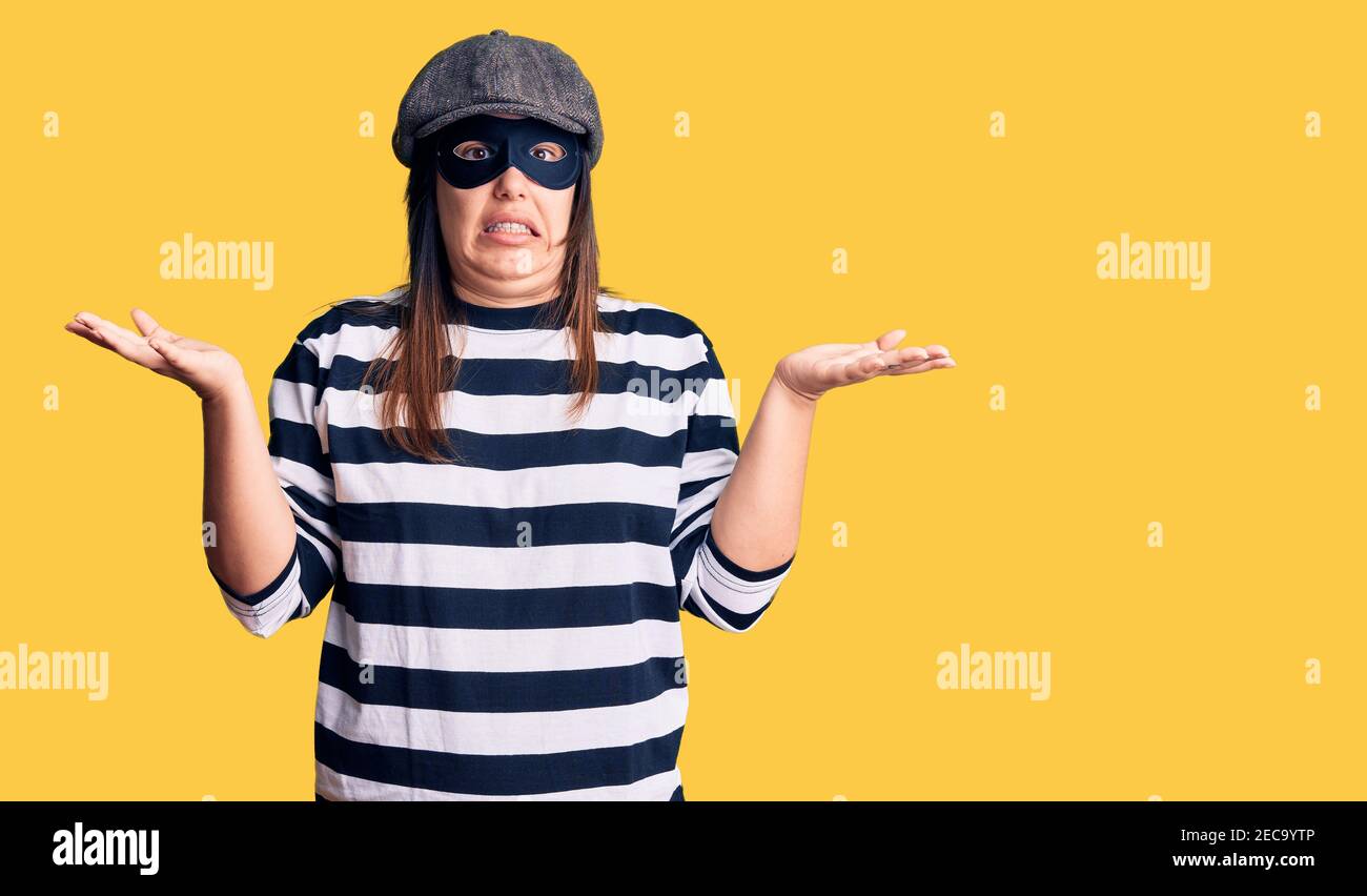 Young beautiful brunette woman wearing burglar mask clueless and ...