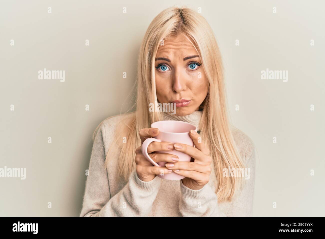 Young blonde woman drinking a cup of coffee depressed and worry for ...