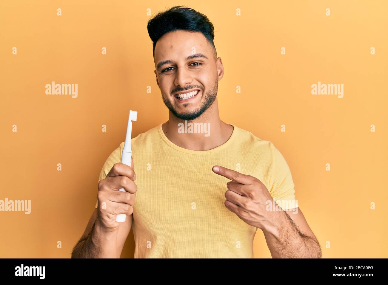 Young arab man holding electric toothbrush smiling happy pointing with ...