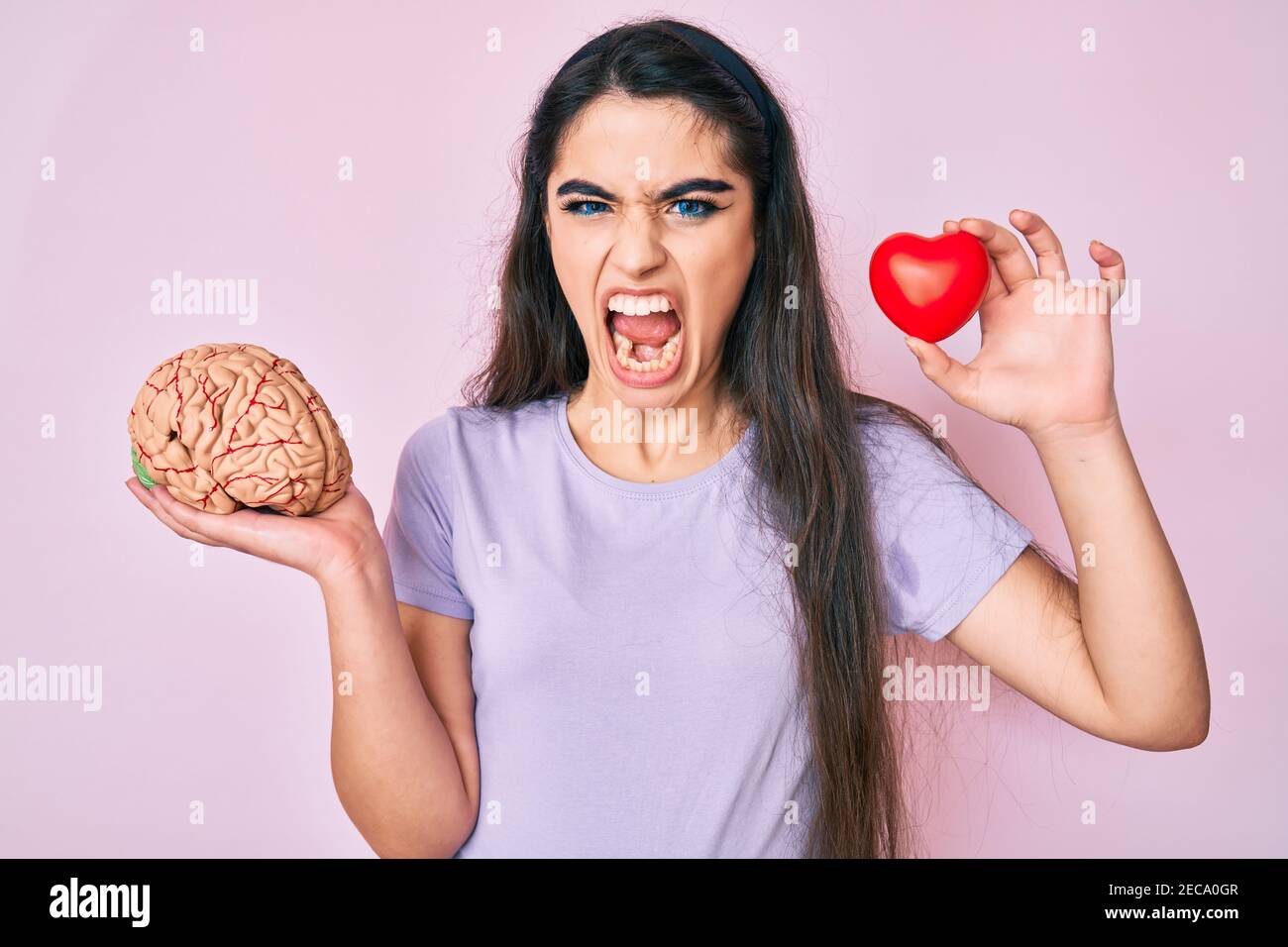 Brunette teenager girl holding brain and heart angry and mad screaming ...