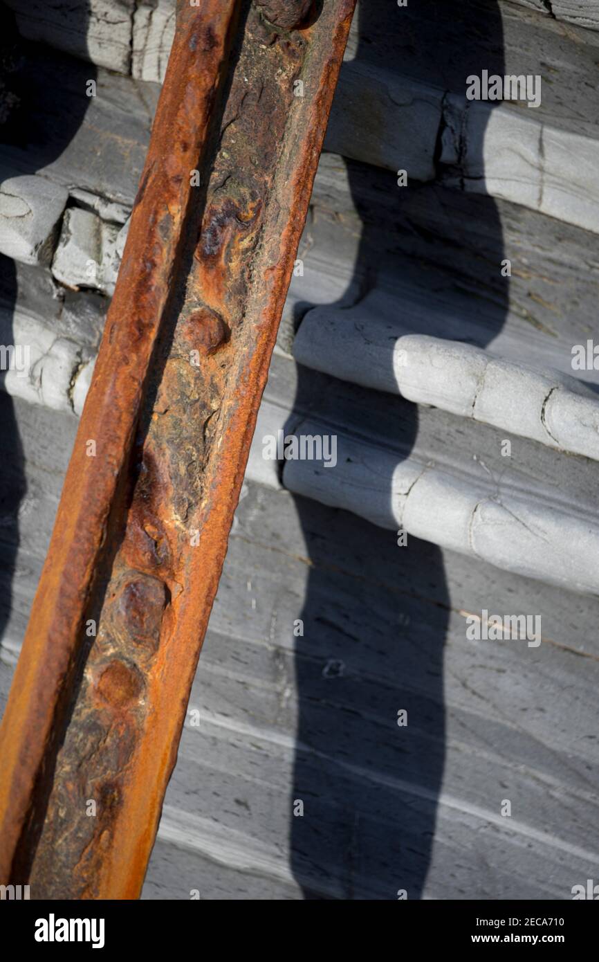 Beach with stacked limestone strata and rusty metal frame in Ceredigion ...