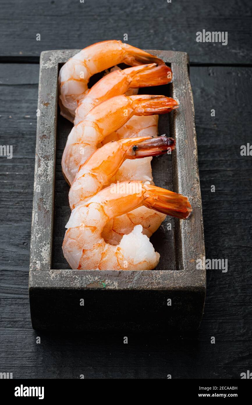 Peeled giant prawns with tails set, in wooden box, on black wooden ...