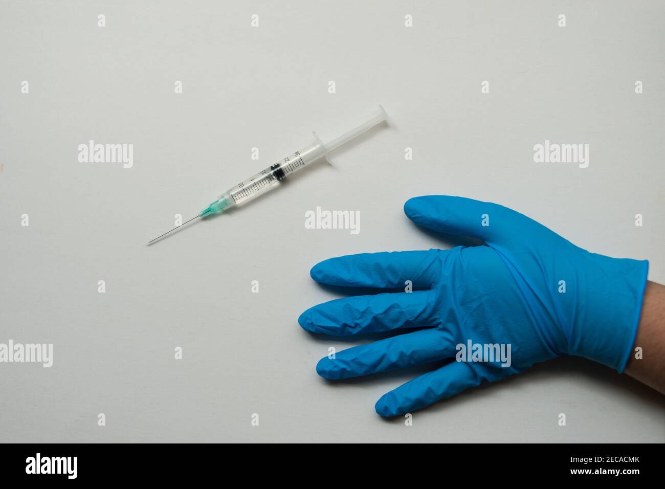 Hand wearing a blue medical glove using a injection on a white surface ...
