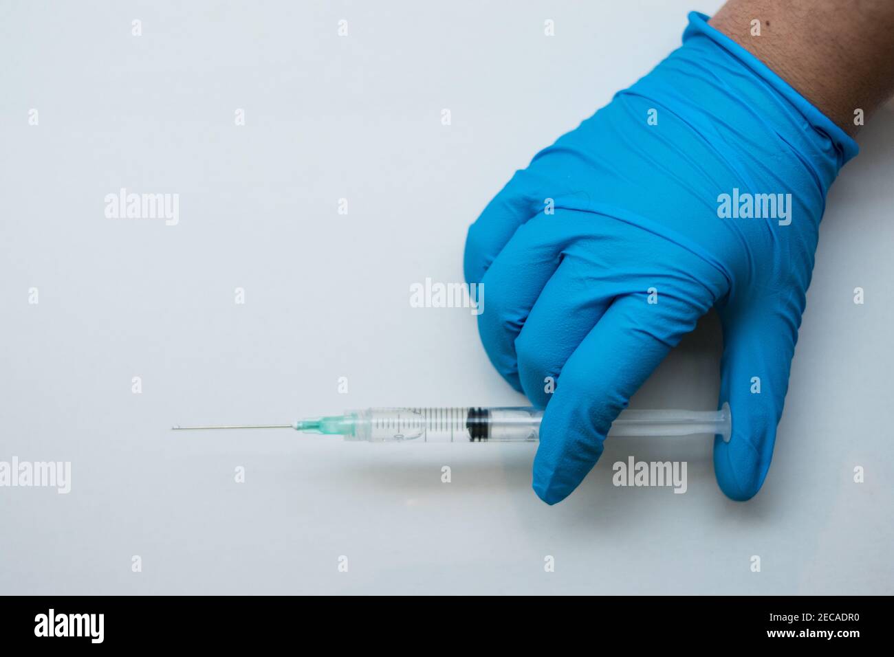 Hand wearing a blue medical glove using a injection on a white surface ...