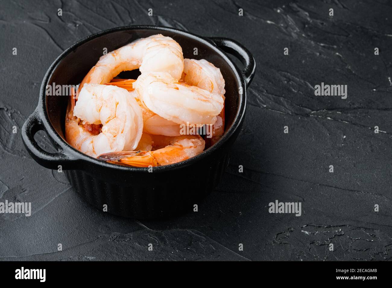 Peeled giant prawns with tails set, in bowl, on black background , with ...