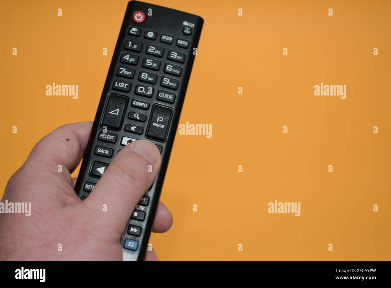 Hand holding black multimedia tv remote control on yellow background ...