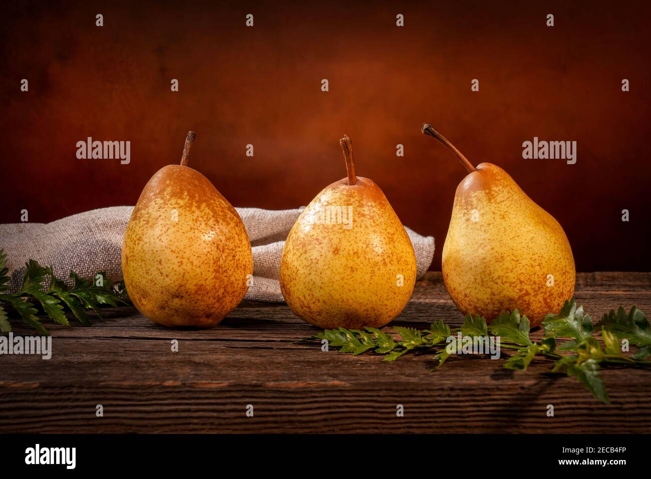 Three yellow pears and a fern on a barn wood table in front of a ...