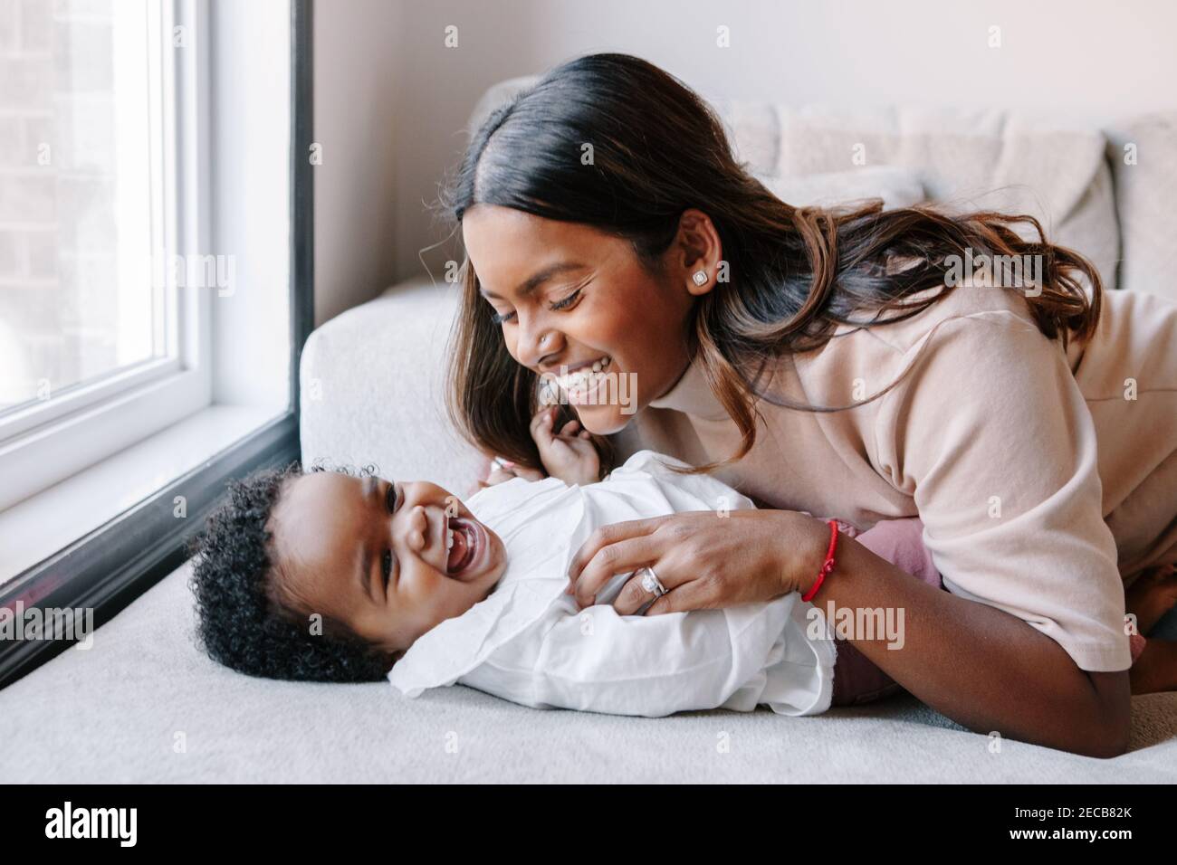 Happy smiling laughing Indian mother playing with black baby girl daughter. Family mixed race ...