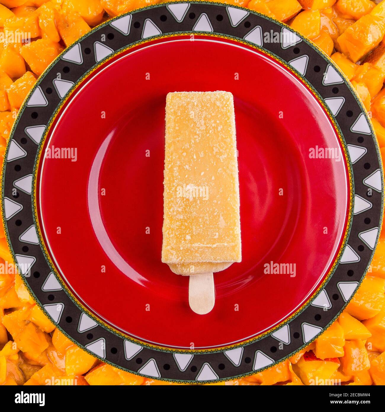 A mango Mexican paleta (popsicle) on a red plate with chopped mango ...