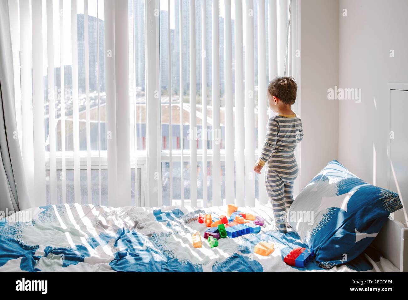 Cute little boy toddler standing on bed in room and looking into window ...