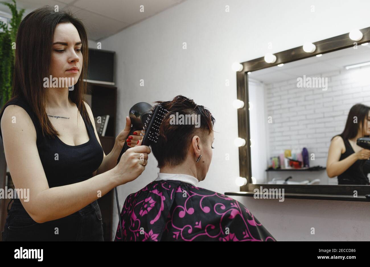 a girl hairdresser makes a hairstyle for a woman client in a modern ...