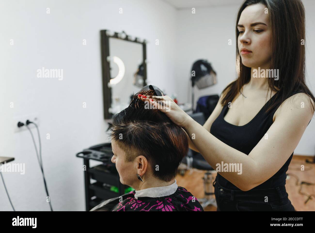 a girl hairdresser makes a hairstyle for a woman client in a modern ...