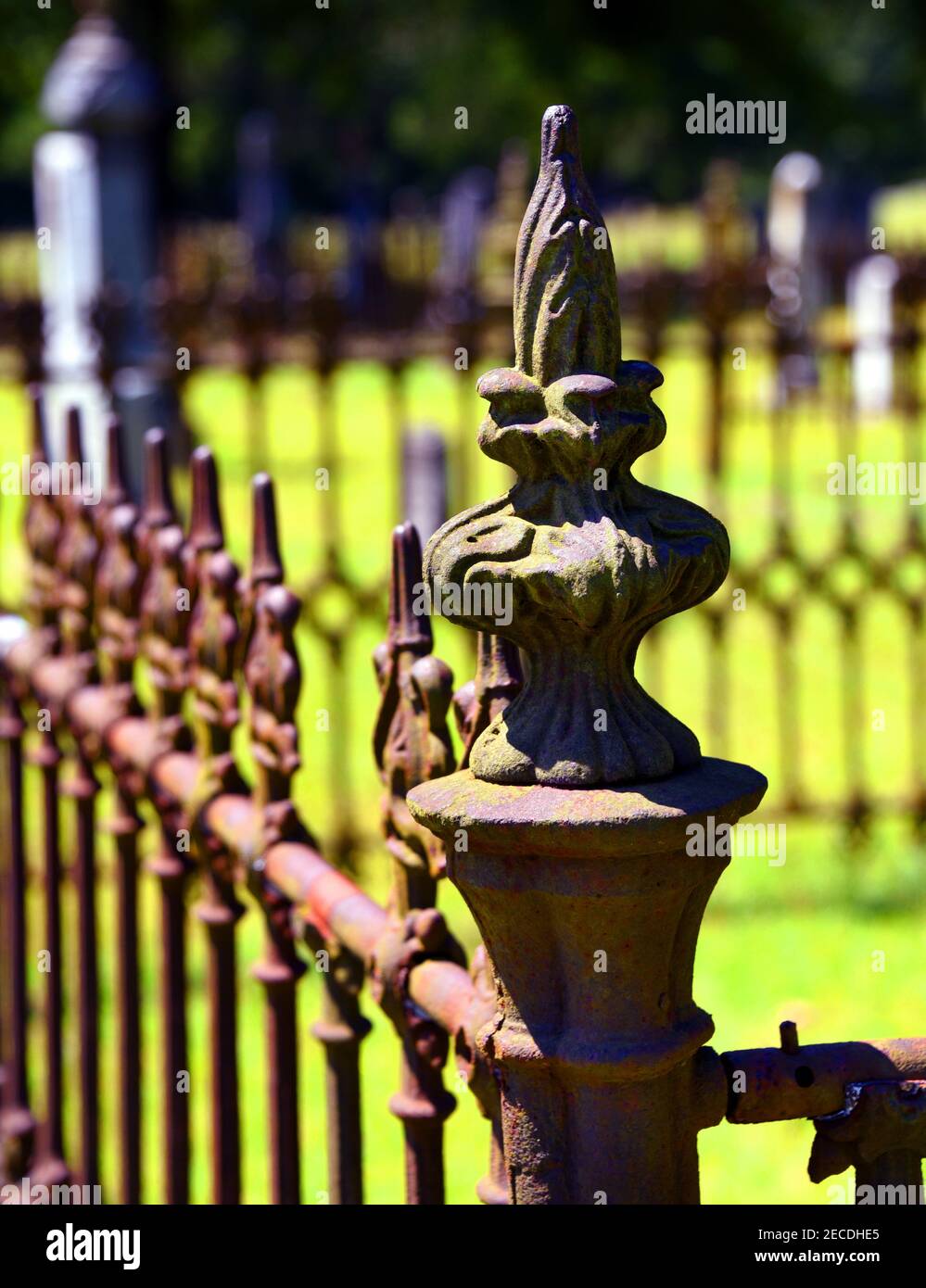 Rustic iron fence surrounds graves at a cemetery. It is rusting but ...