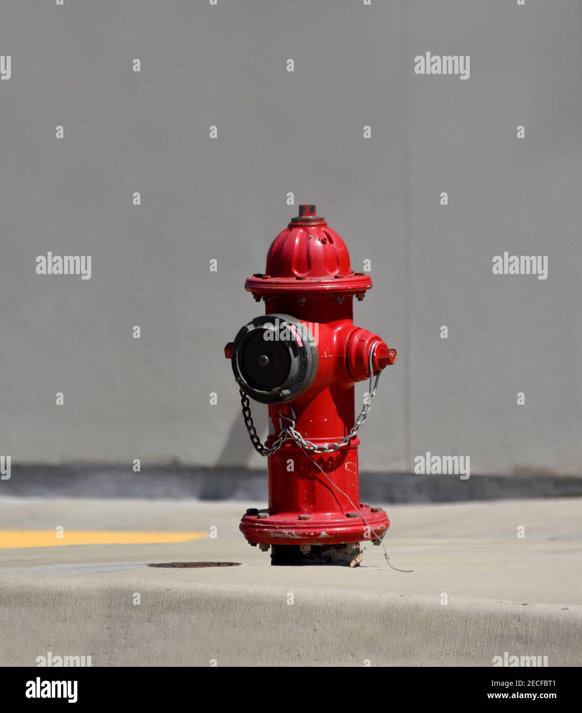 Bright red fire hydrant sits on the curb side. Blank wall sits behind ...