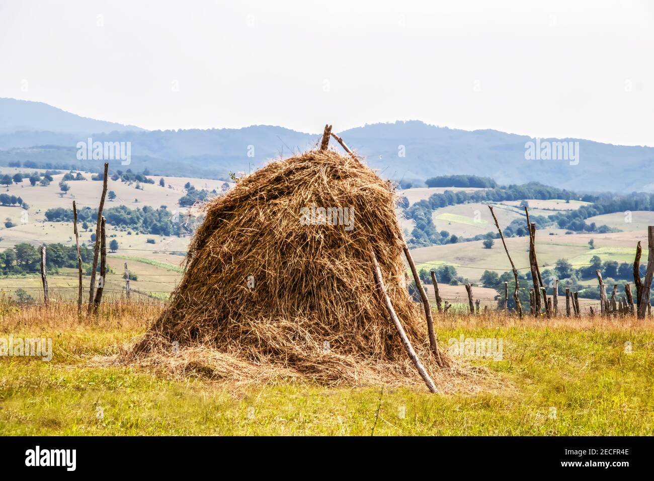 Old fashioned hay stack surrounded by stick fence with farm and hill ...