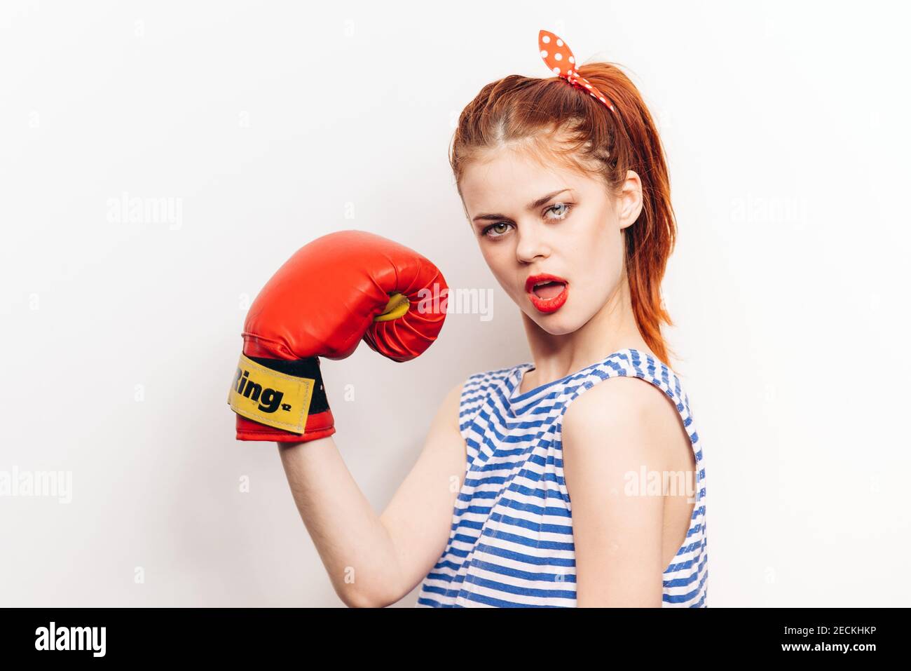 active woman boxing in red gloves and a striped t-shirt on a light ...