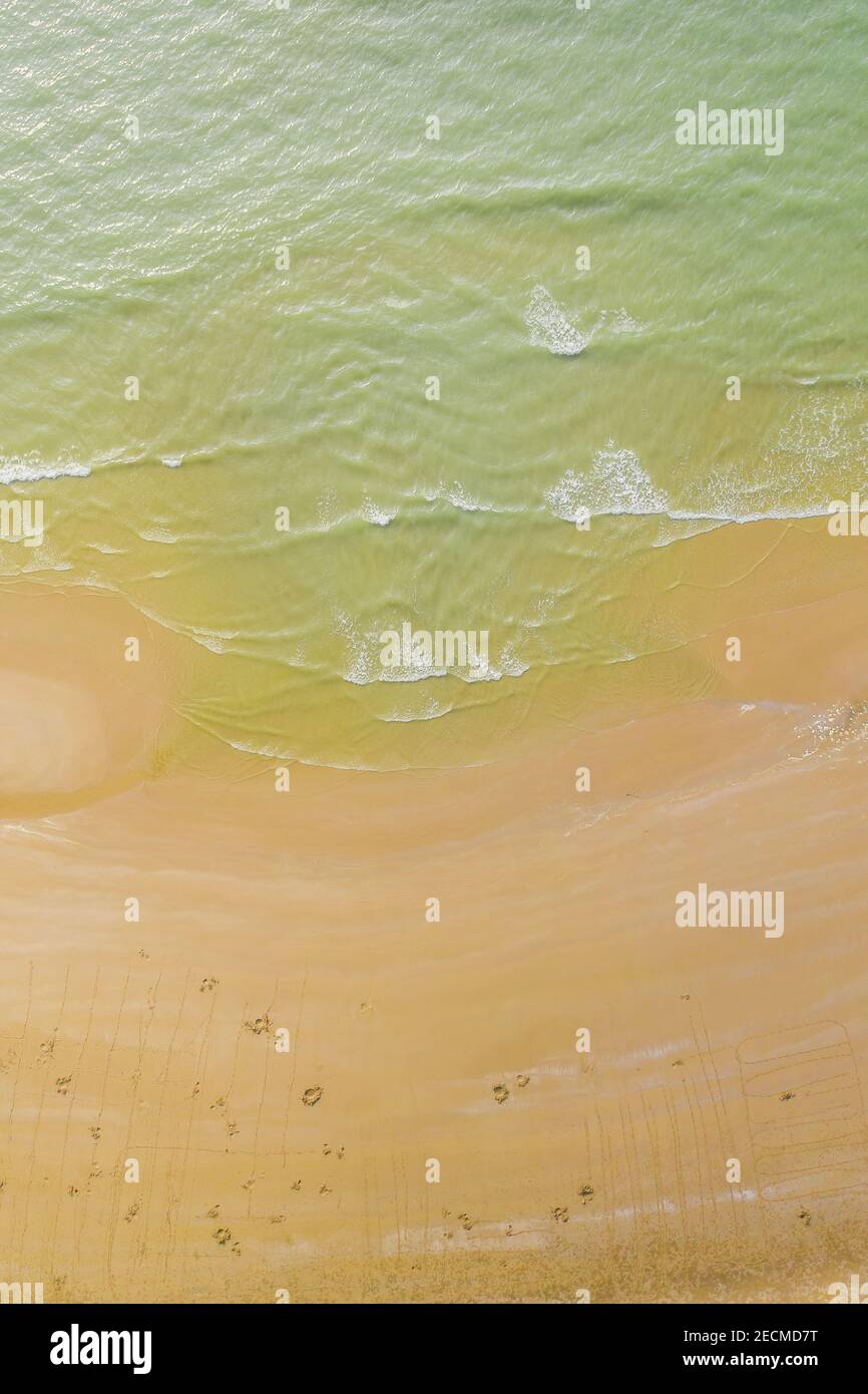 An aerial view of the wavy ocean hitting the sandy beach on the coast ...