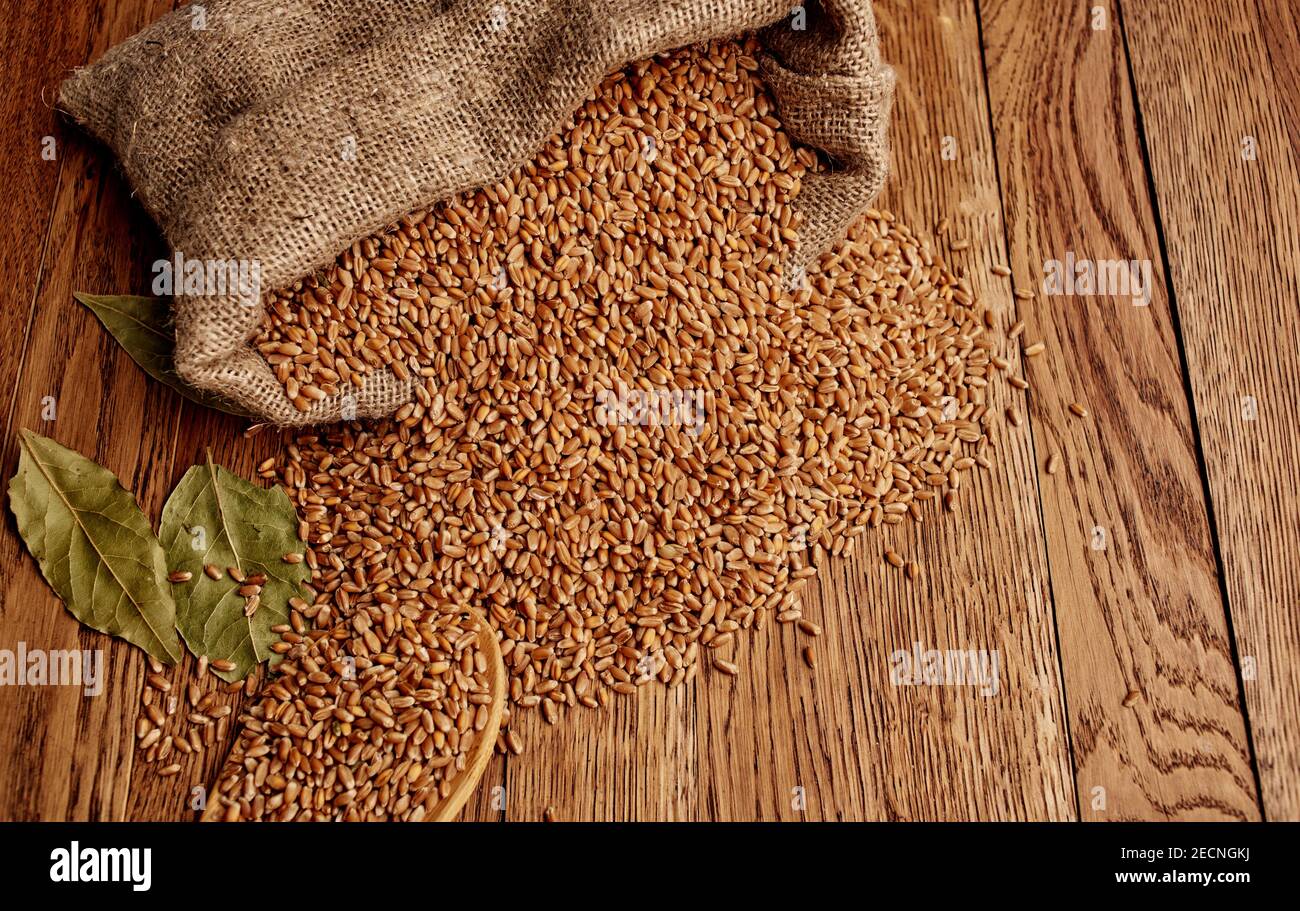 Wheat in a bag on a wooden table and dry leaves organic texture ...
