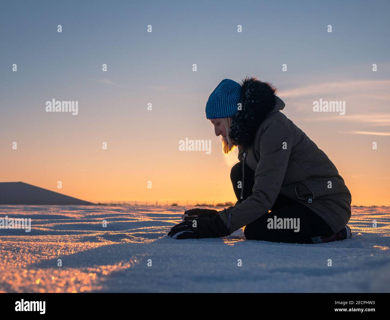 A woman crouching down and collecting snow in a beautiful snow field ...