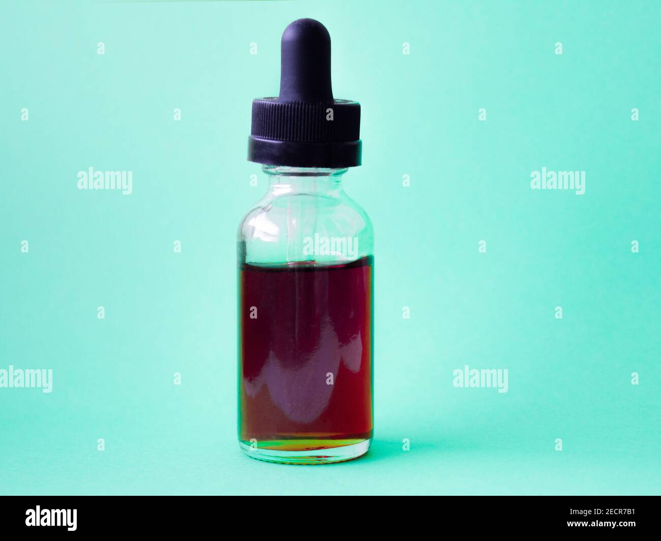 Dark red liquid in a glass bottle with a pipette on a bright green ...