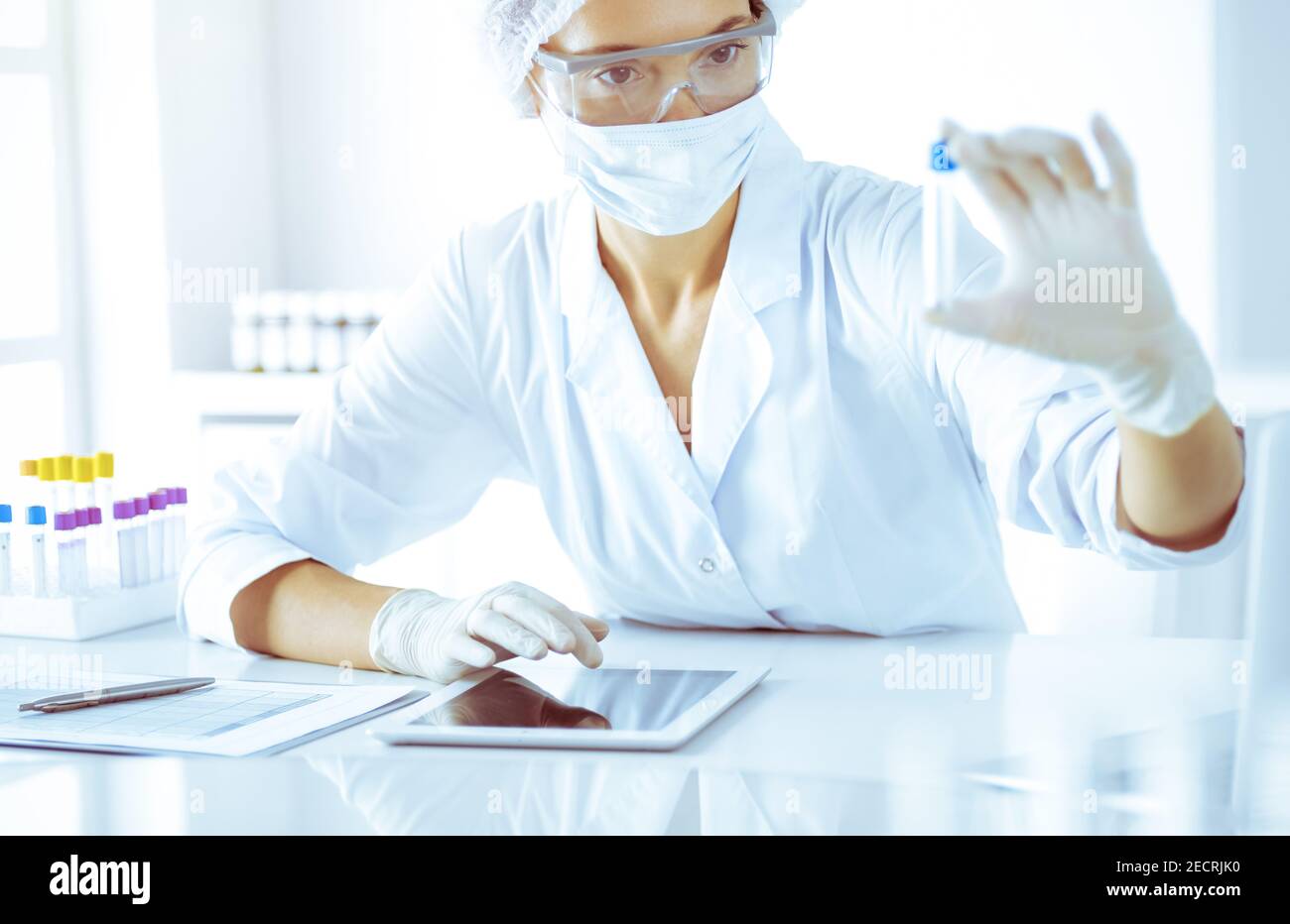 Professional female scientist in protective eyeglasses researching tube ...