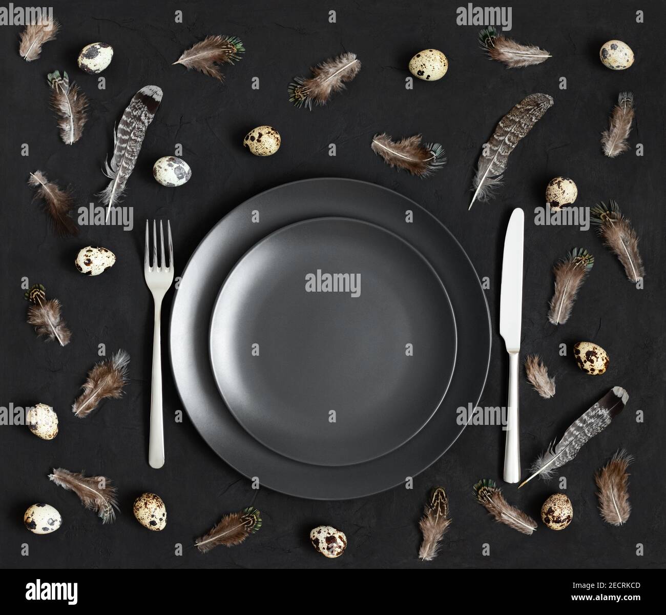 Table setting with a black plate, quail eggs and feathers on a black ...