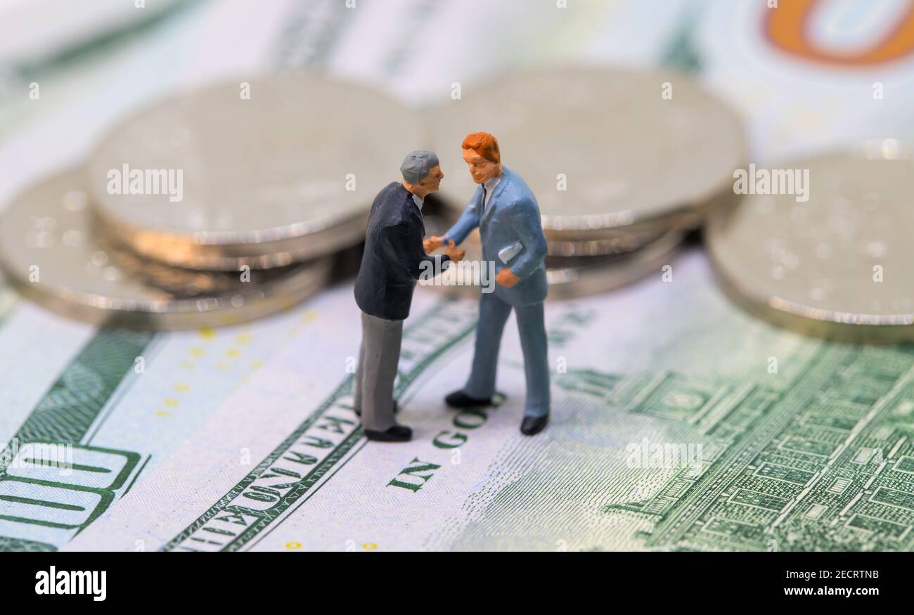Businessmen toy shaking hands on cash. Tiny businessmen figurines on ...