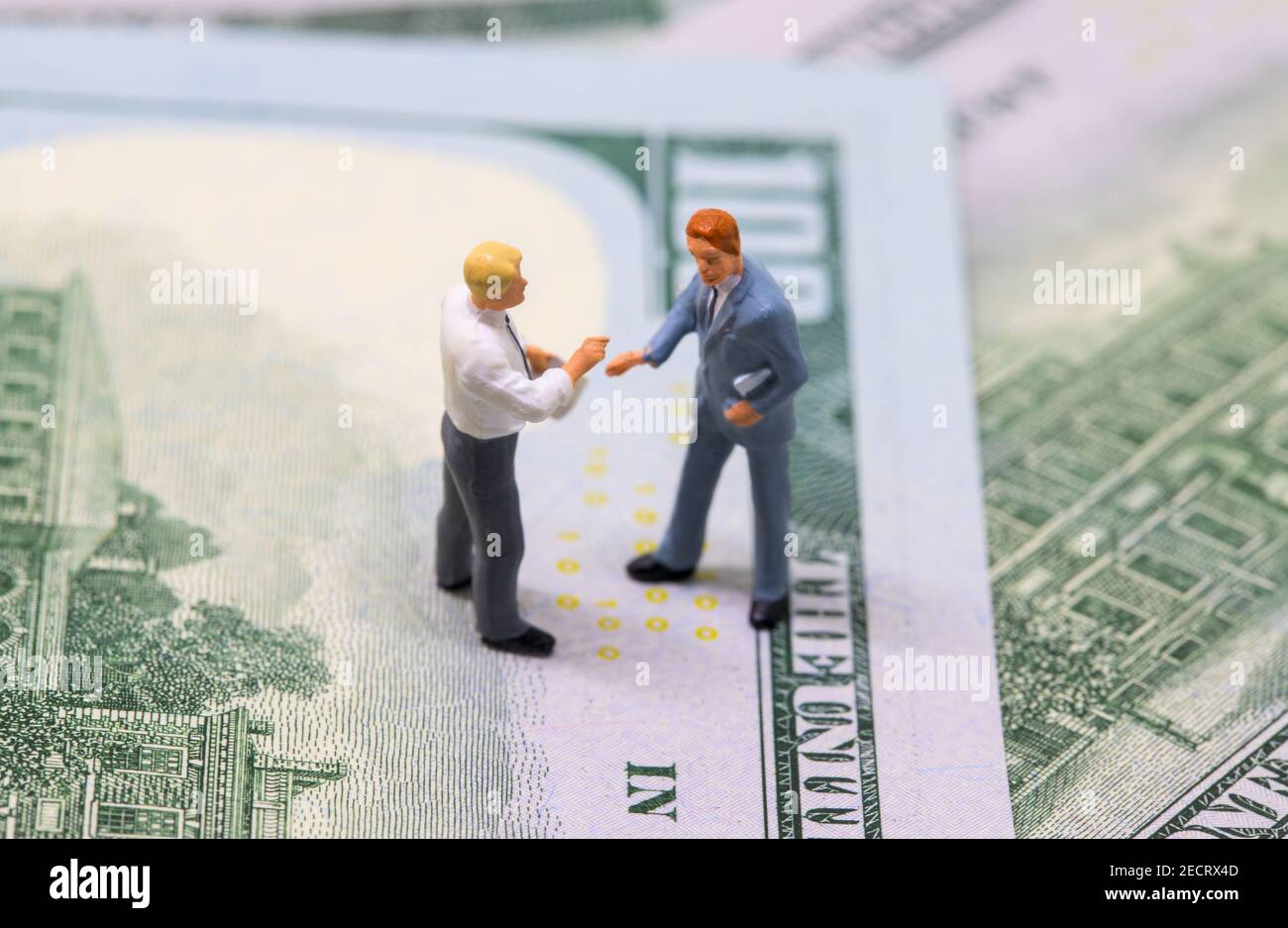 Businessmen figurines shaking hands on cash. Tiny businessmen models on ...