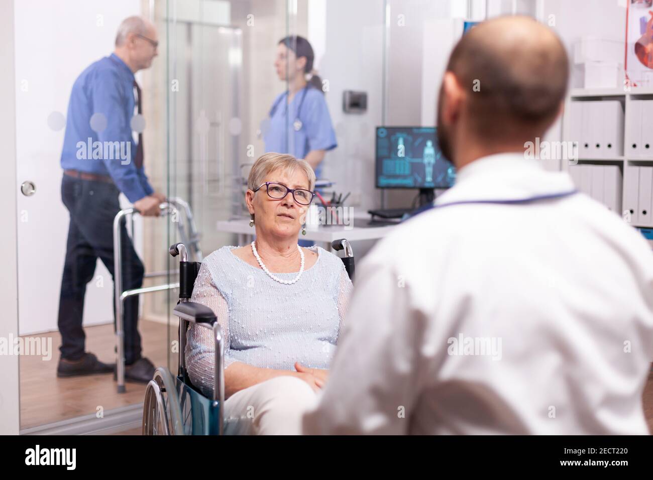 Handicapped senior patient in wheelchair talking with doctor in ...