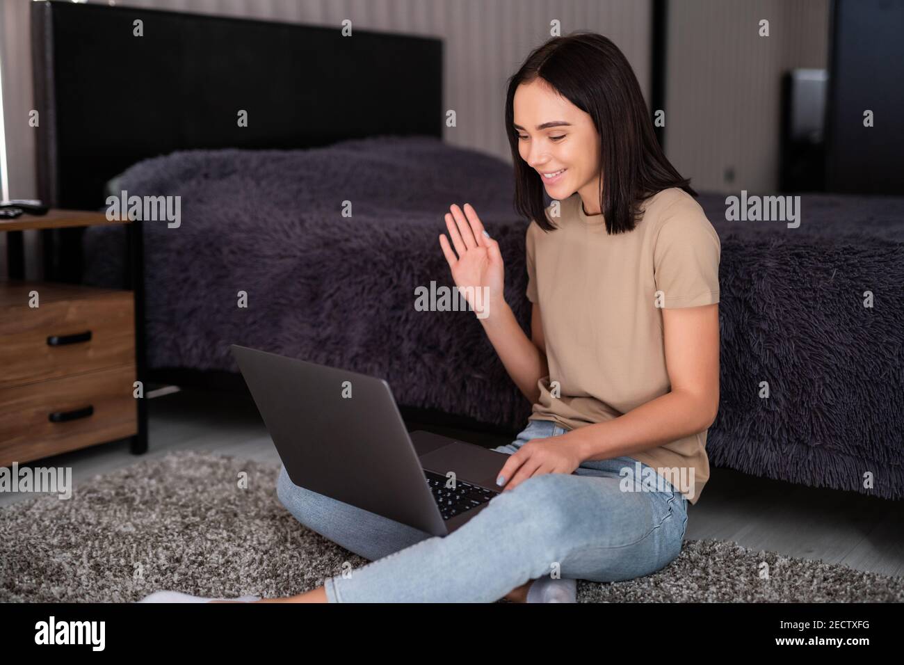 Cheerful woman having a videocall while sitting on a floor with laptop ...