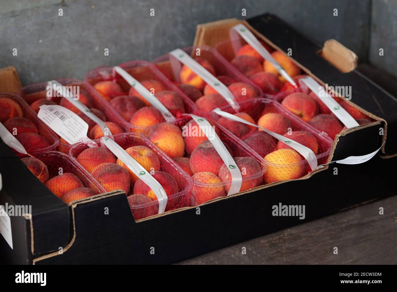Plenty of fresh peaches in kilogram packs inside a black cardboard box ...