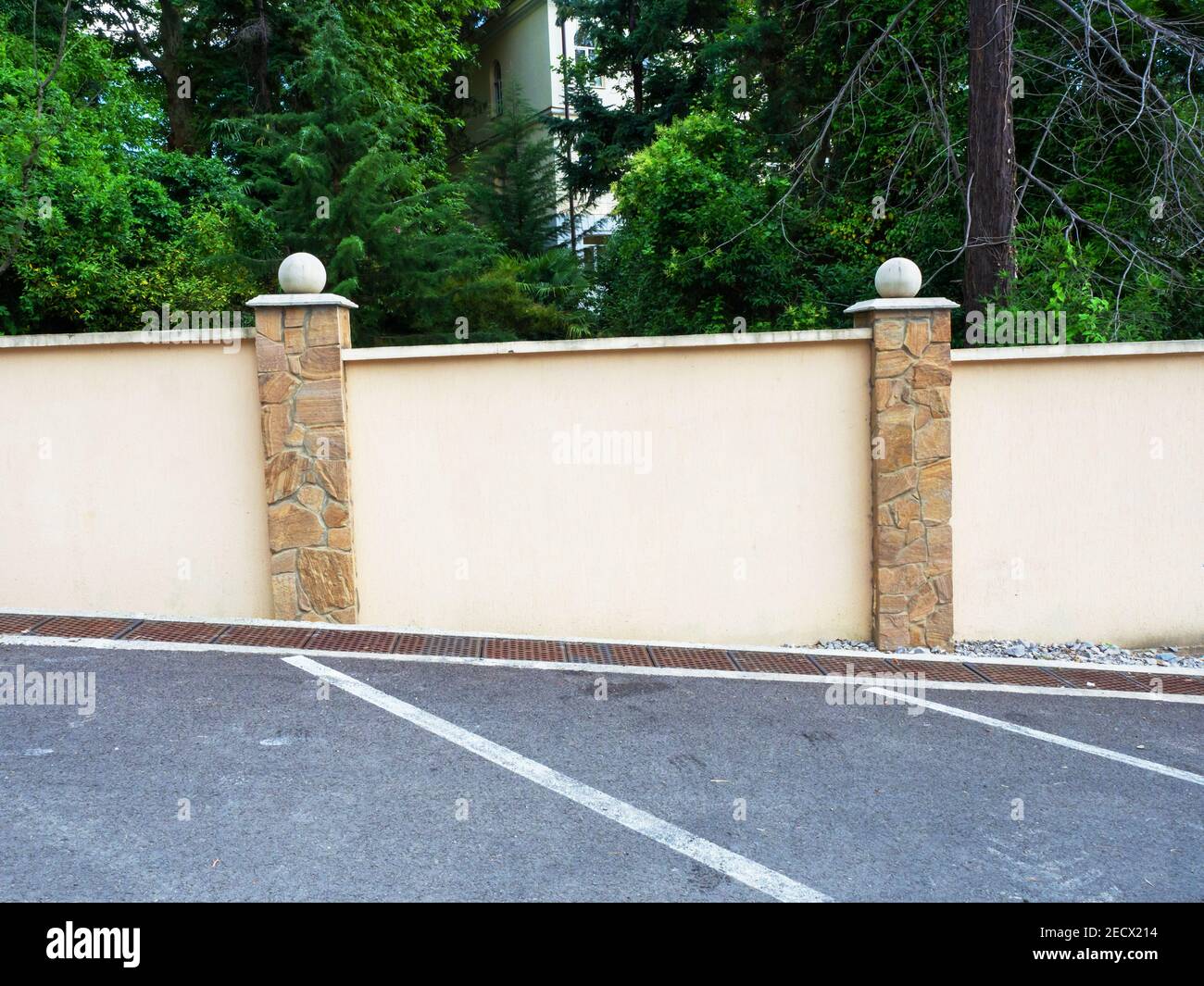 A fence running along marked asphalt road section and green trees and a ...