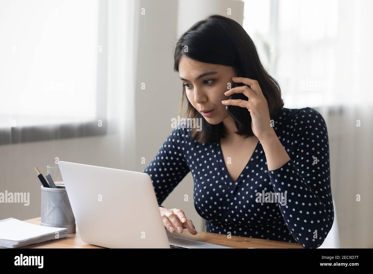 Vietnamese female consulting client by cell looking at pc screen Stock ...