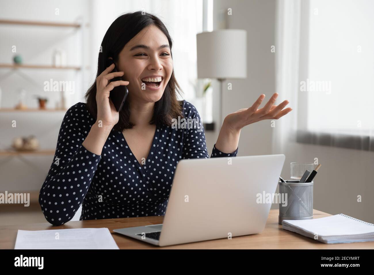 Overjoyed asian female telling story by phone before computer screen ...